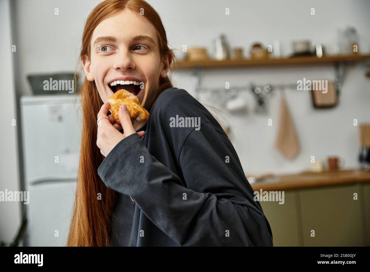 A stylish guy with long hair smiles while taking a bite of a pastry at ...