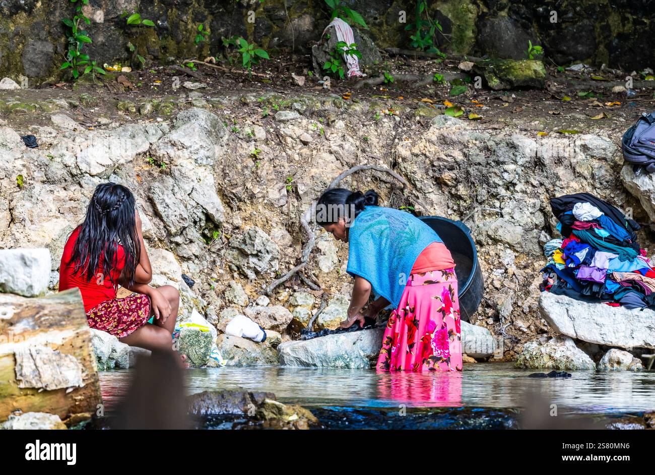 A woman and a girl washing clothes at a natural spring in rural area ...