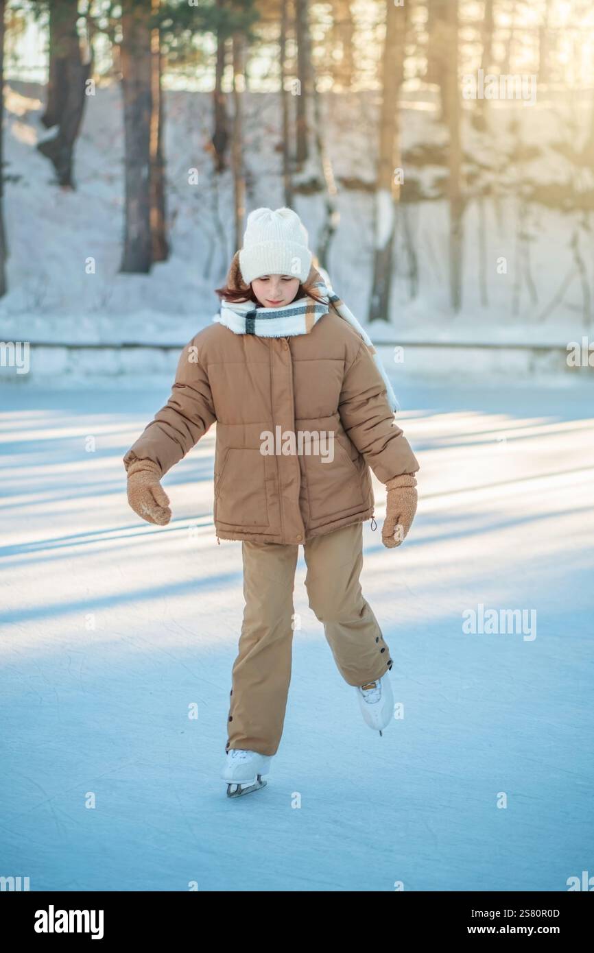 Adorable girl wearing warm winter clothes joyfully ice skating on a ...
