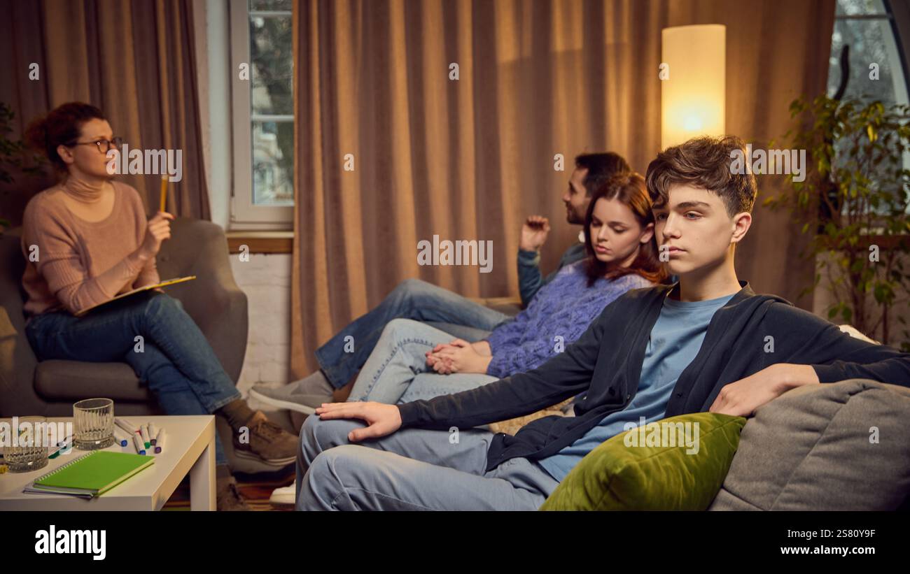 Focus on teen boy reflects during family therapy session with his parents and psychologist ...