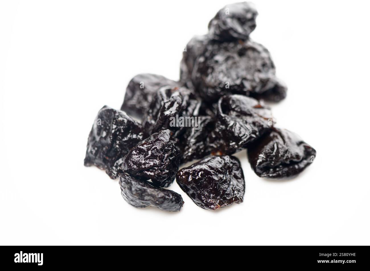 Dark, wrinkled dried plums lie atop a clean, white background ...