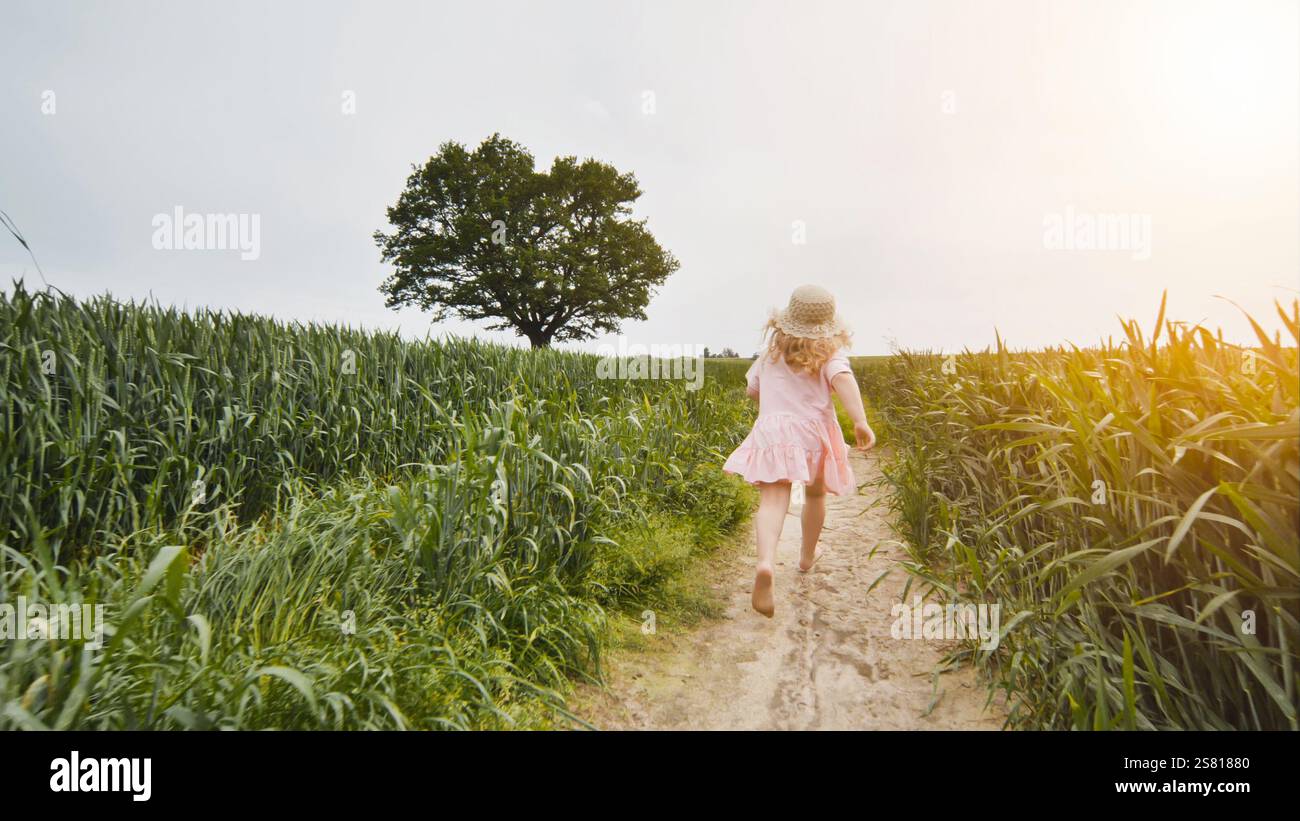 Young girl barefoot running across verdant meadow, reaching solitary ...