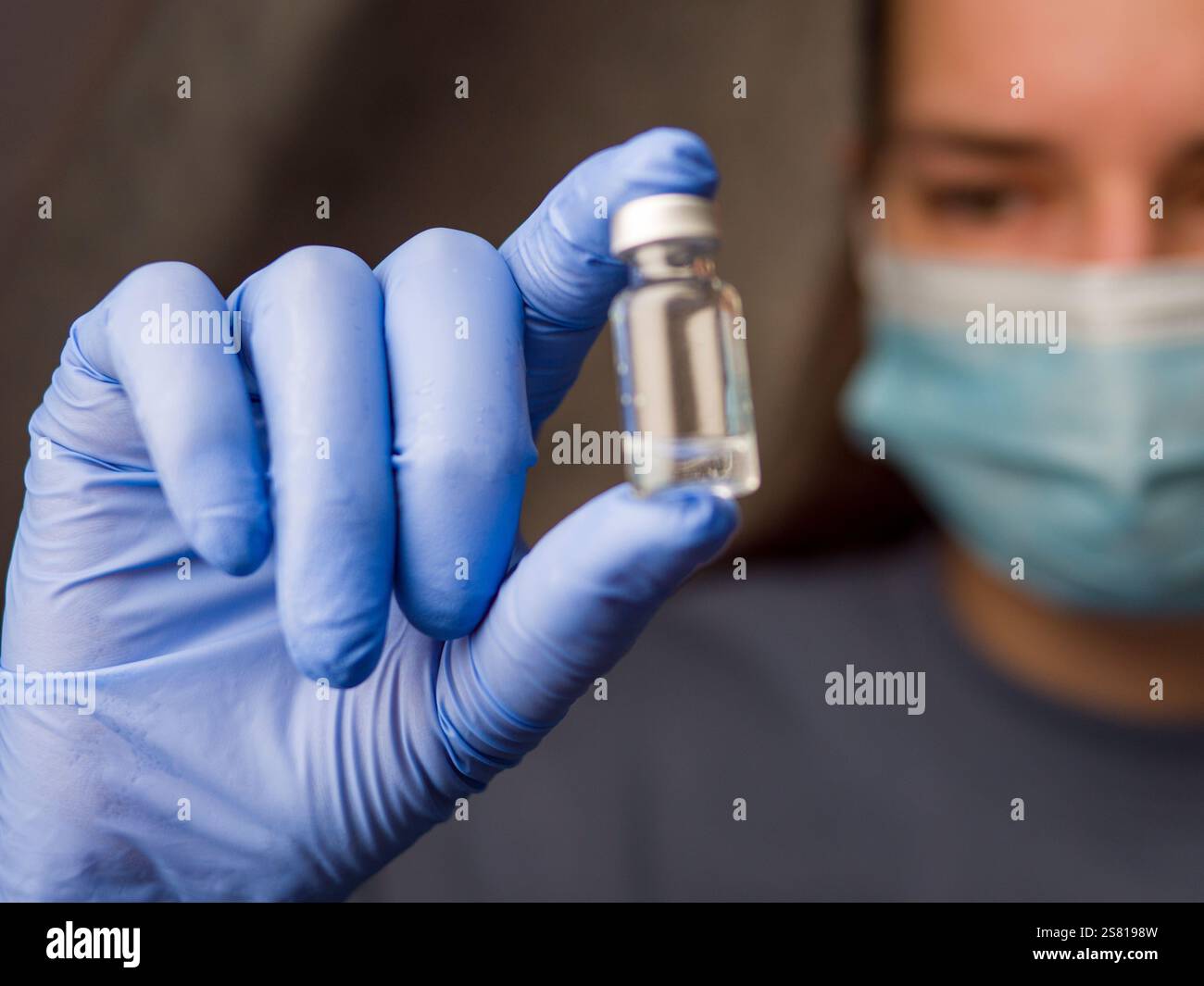 Medical professional examining clear liquid vial, wearing blue latex ...