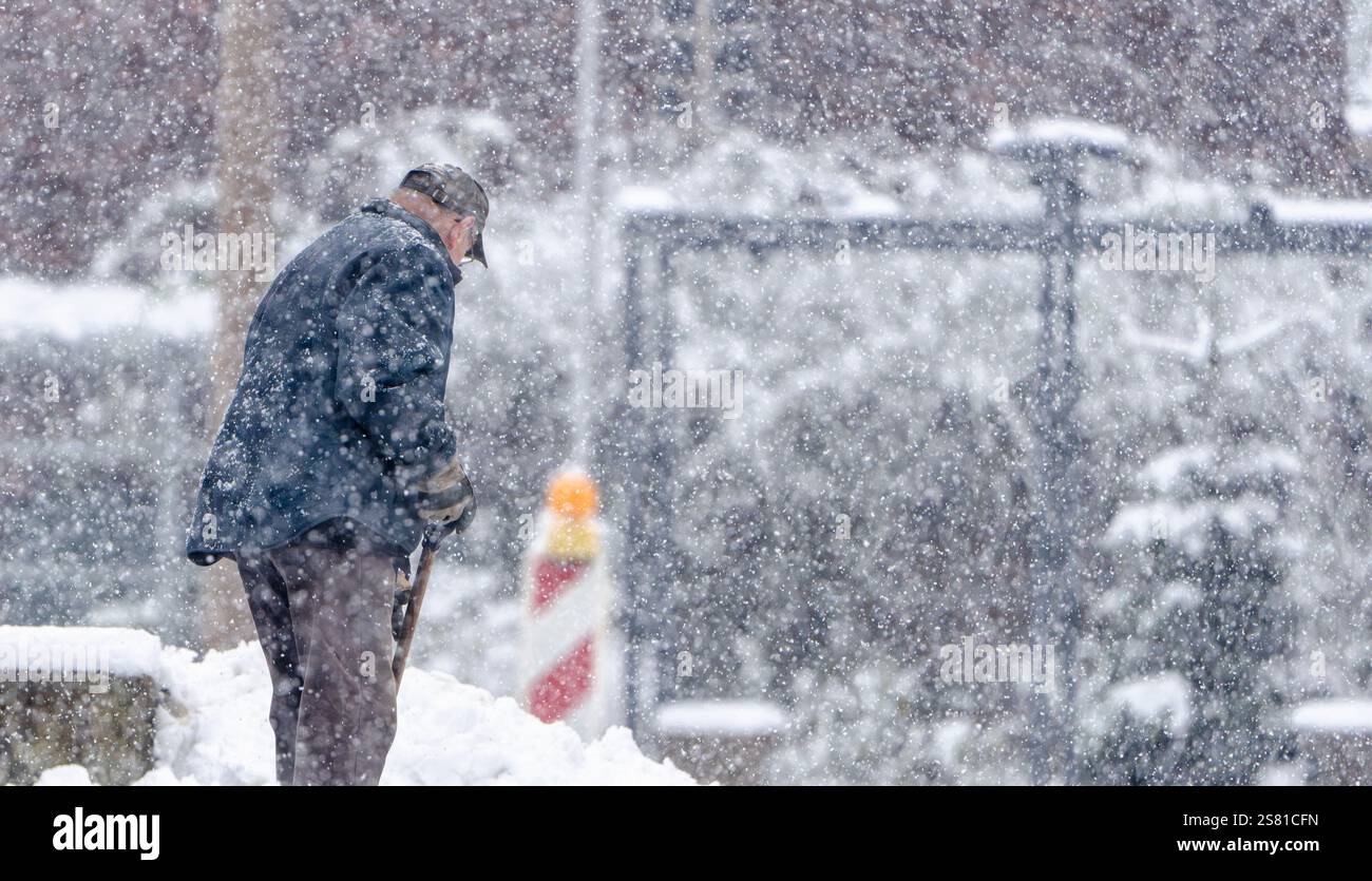 A man is shoveling snow off a sidewalk. The snow is falling and the man ...
