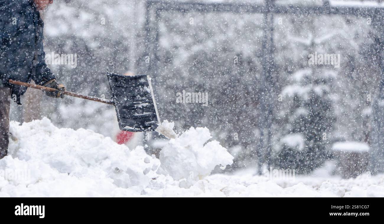 A man is shoveling snow with a black shovel. The snow is falling and ...