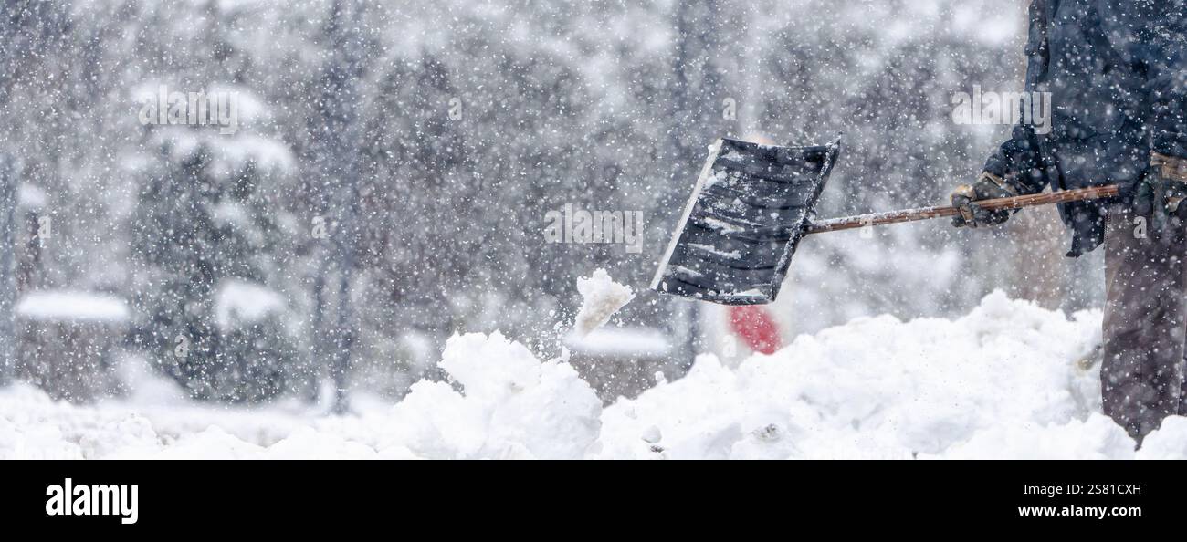 A man is shoveling snow with a snowplow. The snow is falling and the ...