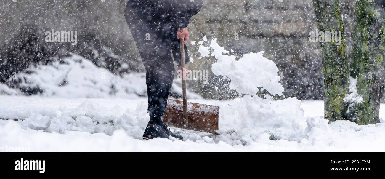 A man is shoveling snow with a snowplow. The snow is falling and the ...