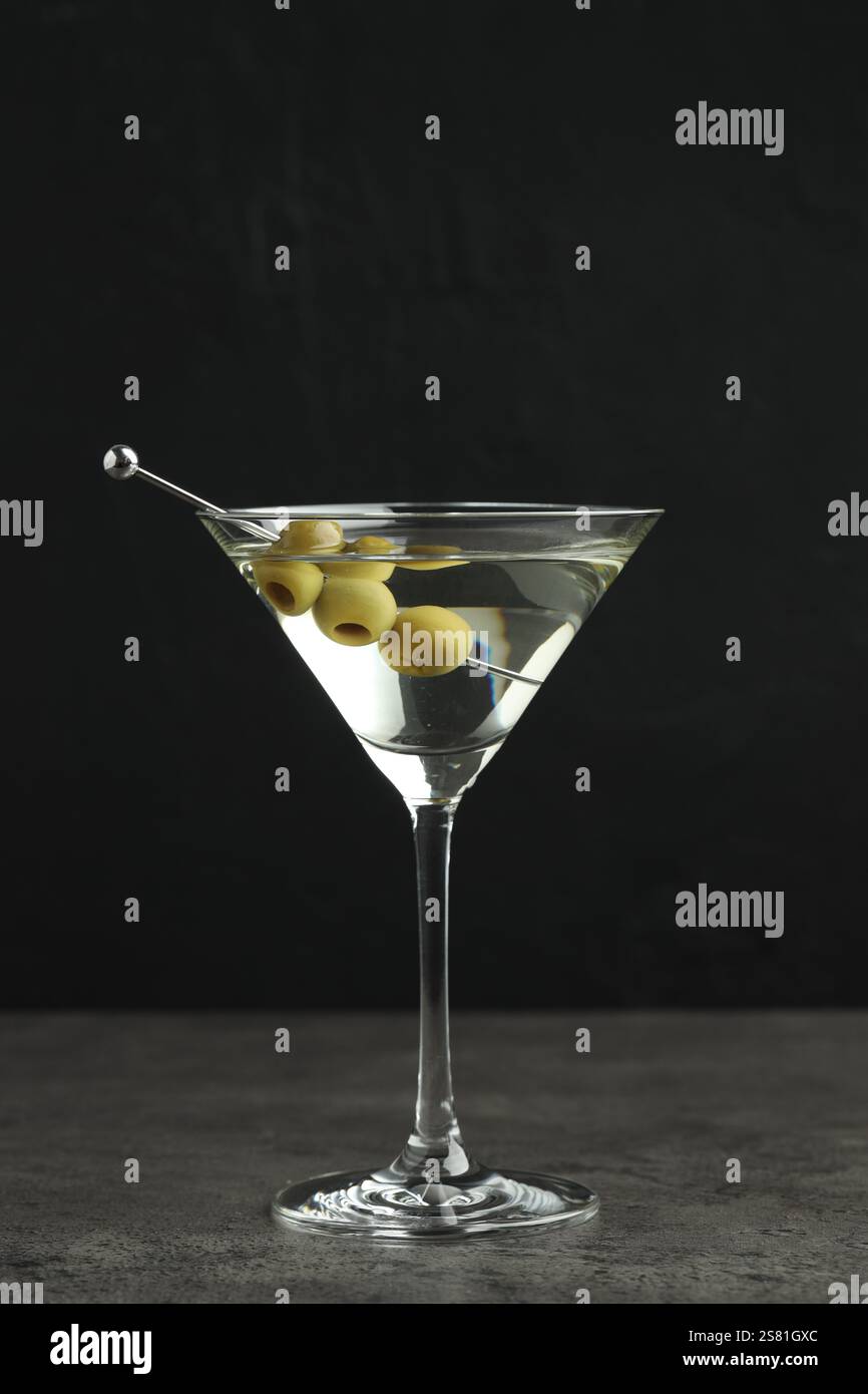 Martini cocktail with olives in glass on grey table against black ...