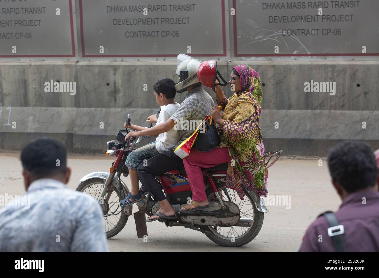 A man and a woman, along with their son, ride on a motorcycle on a busy street in Dhaka. The boy ...