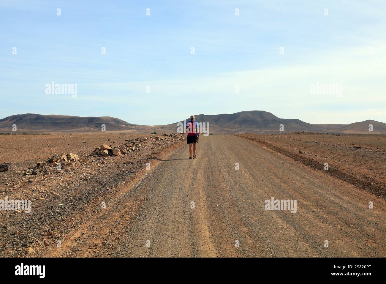 Man with backpack walking away towards distant hills along a dusty ...