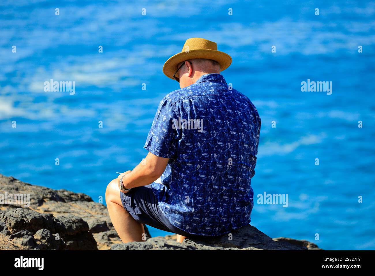 Older man in a straw hat sitting on a cliff overlooking the Atlantic ...