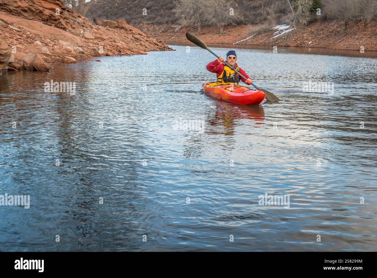 senior male paddler is paddling colorful river kayak on a calm lake ...