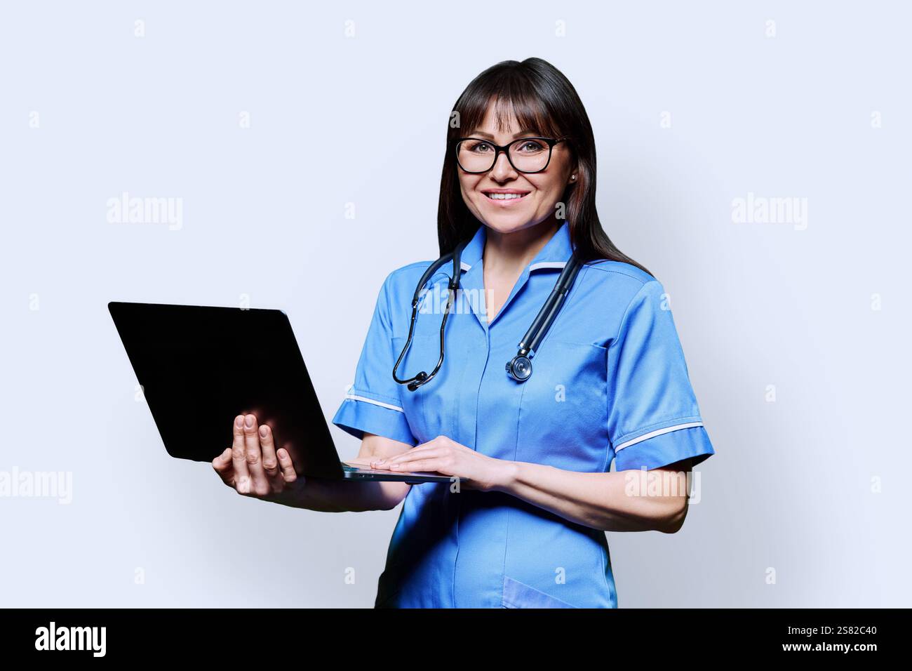 Female nurse holding laptop, looking at camera on white studio ...