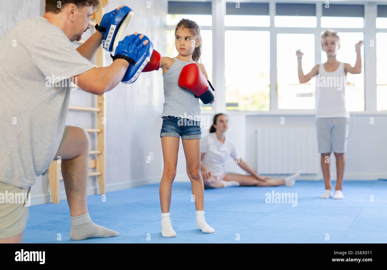 Girl with her trainer father at gym. Boy wearing boxing gloves exercise ...