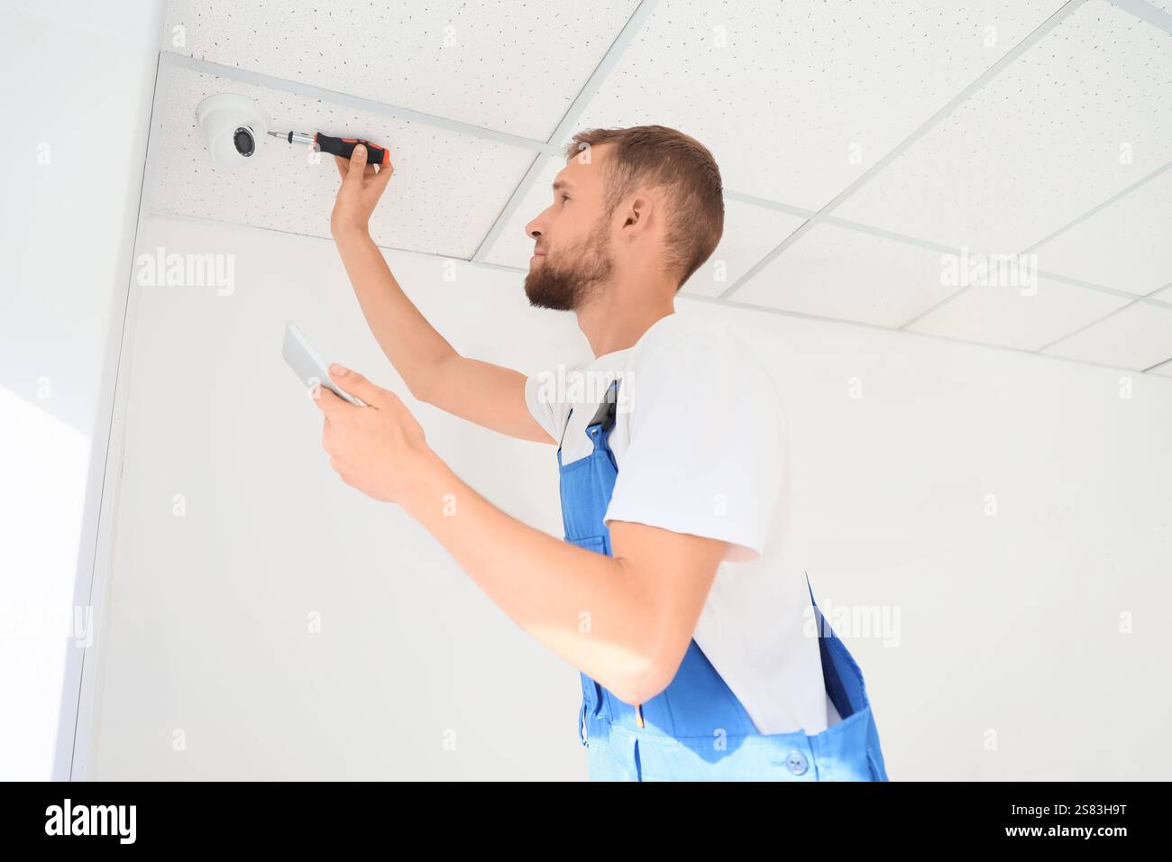 Male worker with tablet computer and screwdriver installing alarm ...