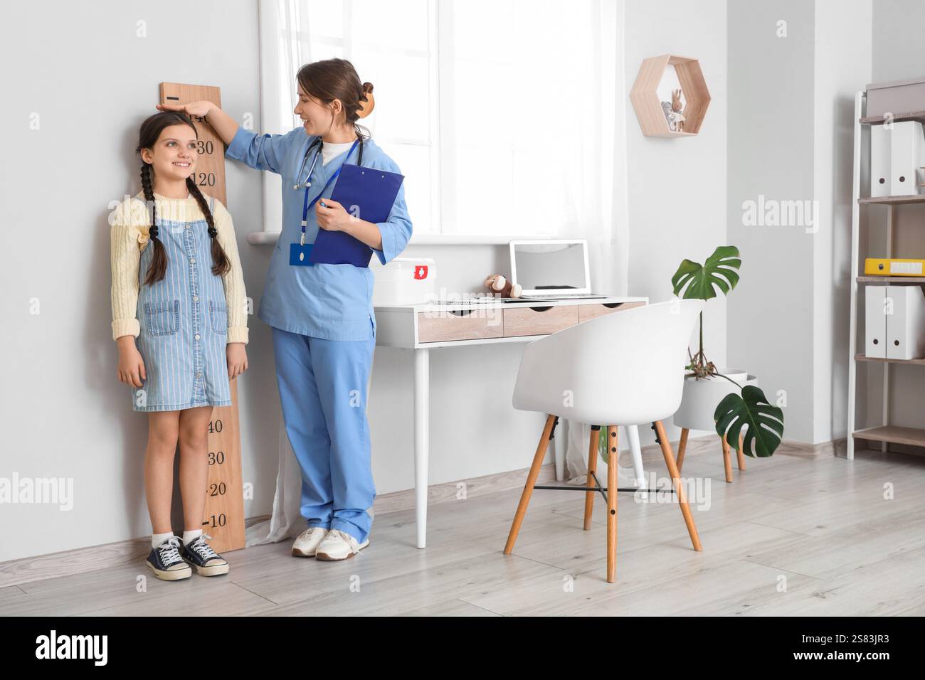 Female pediatrician measuring height of cute girl near stadiometer in ...