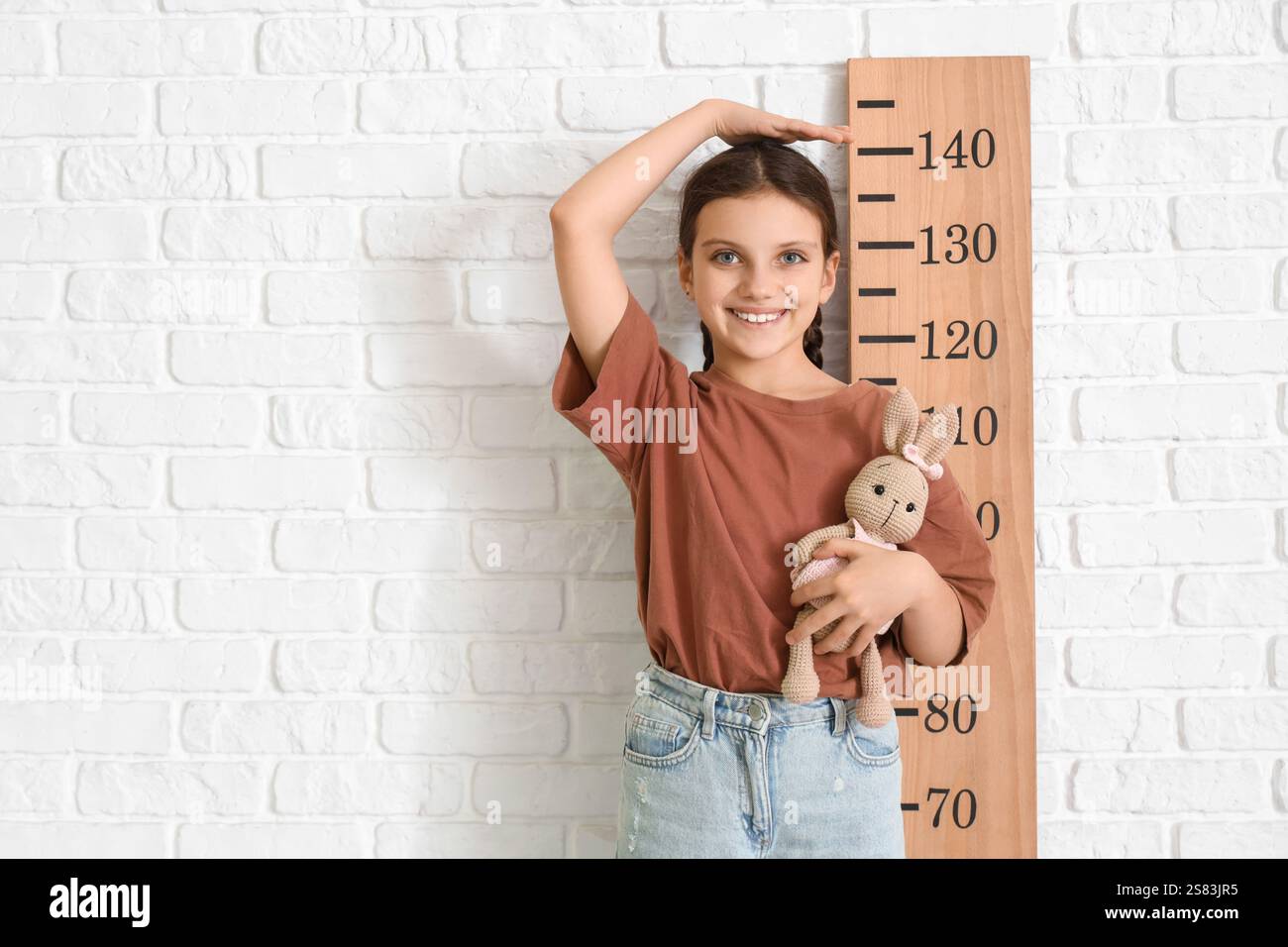 Cute girl measuring height with stadiometer near white brick wall Stock ...