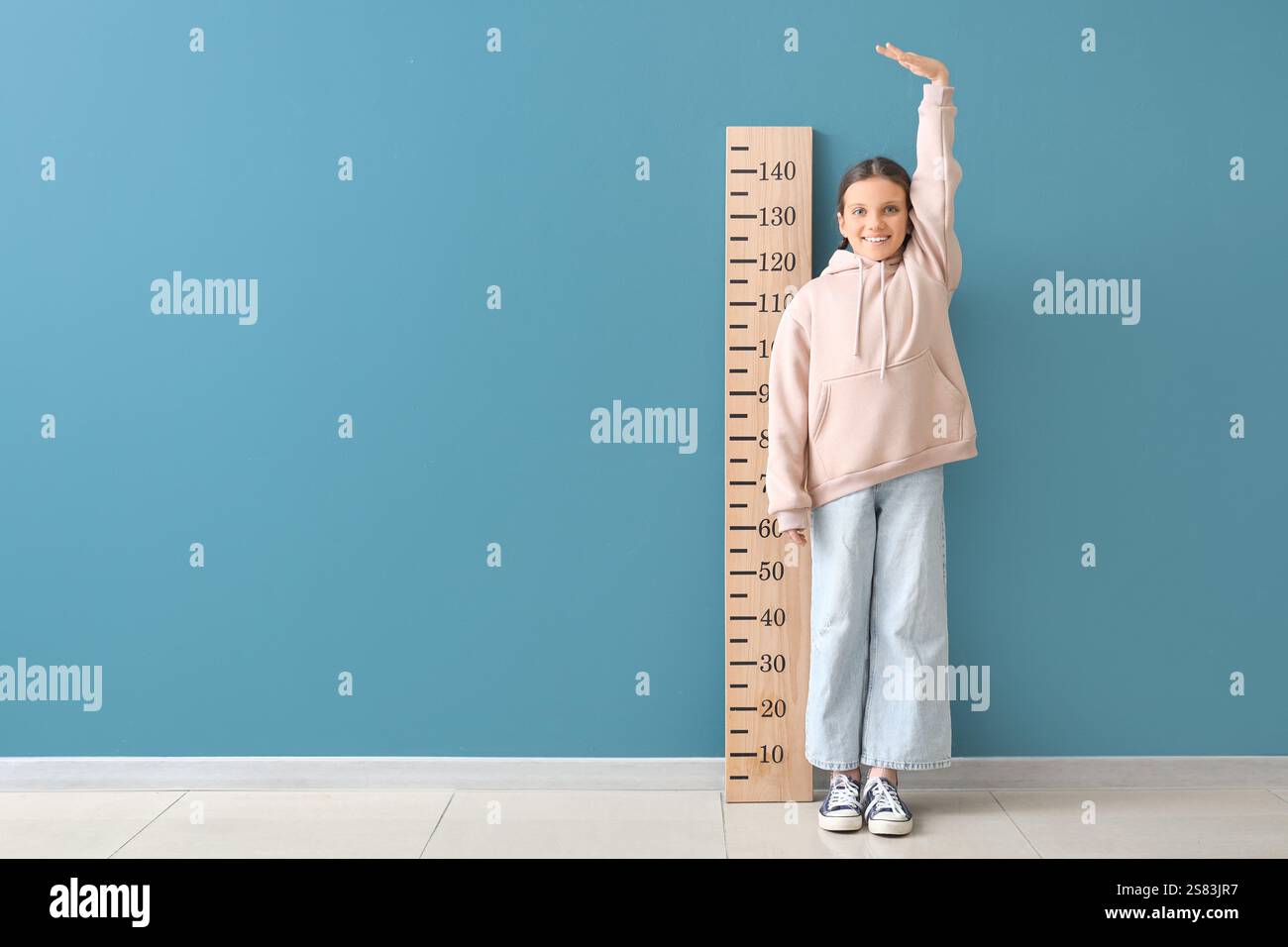 Cute girl measuring height with stadiometer near blue wall Stock Photo ...