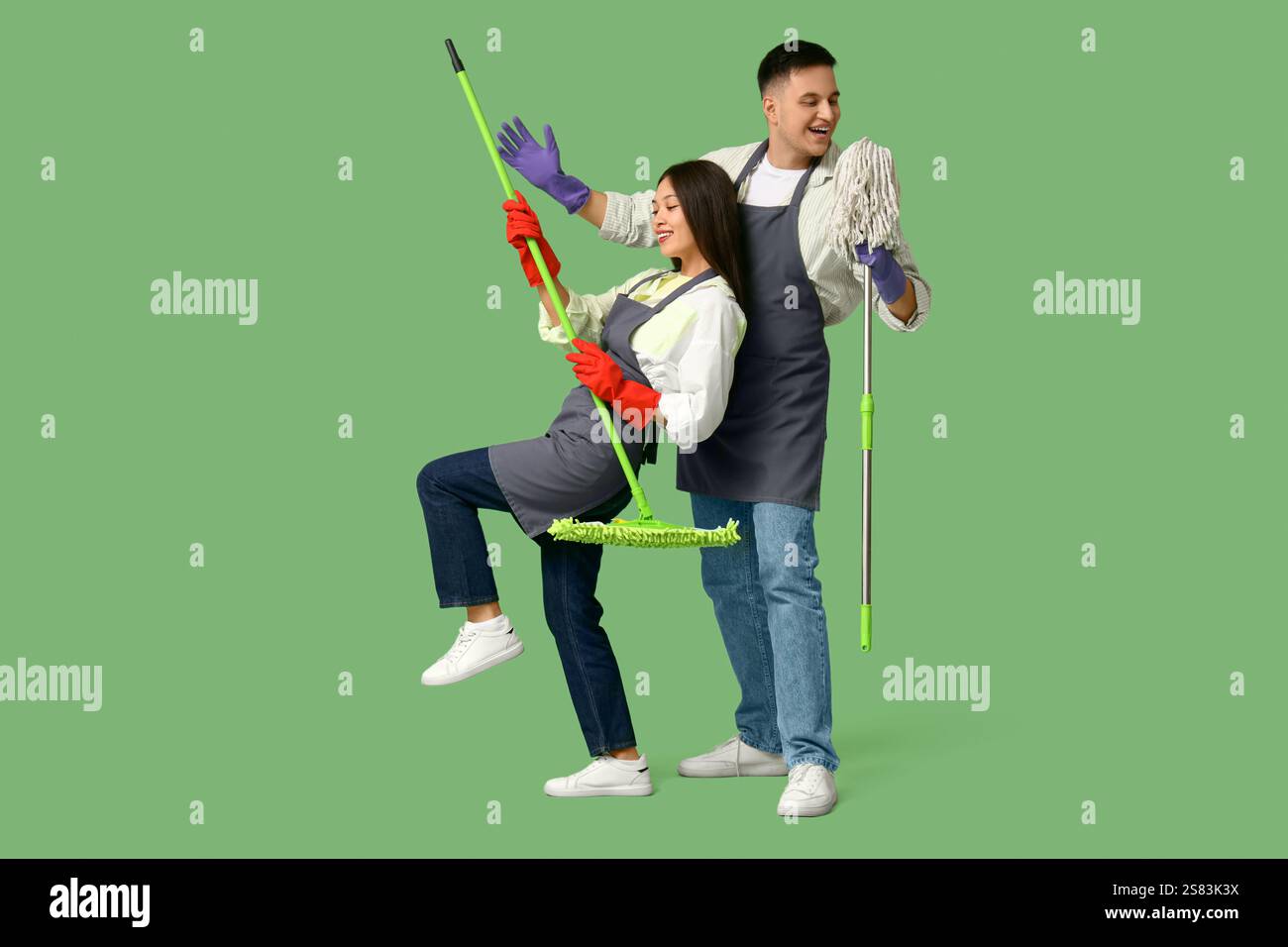Cute young couple having fun with floor mops on green background Stock ...