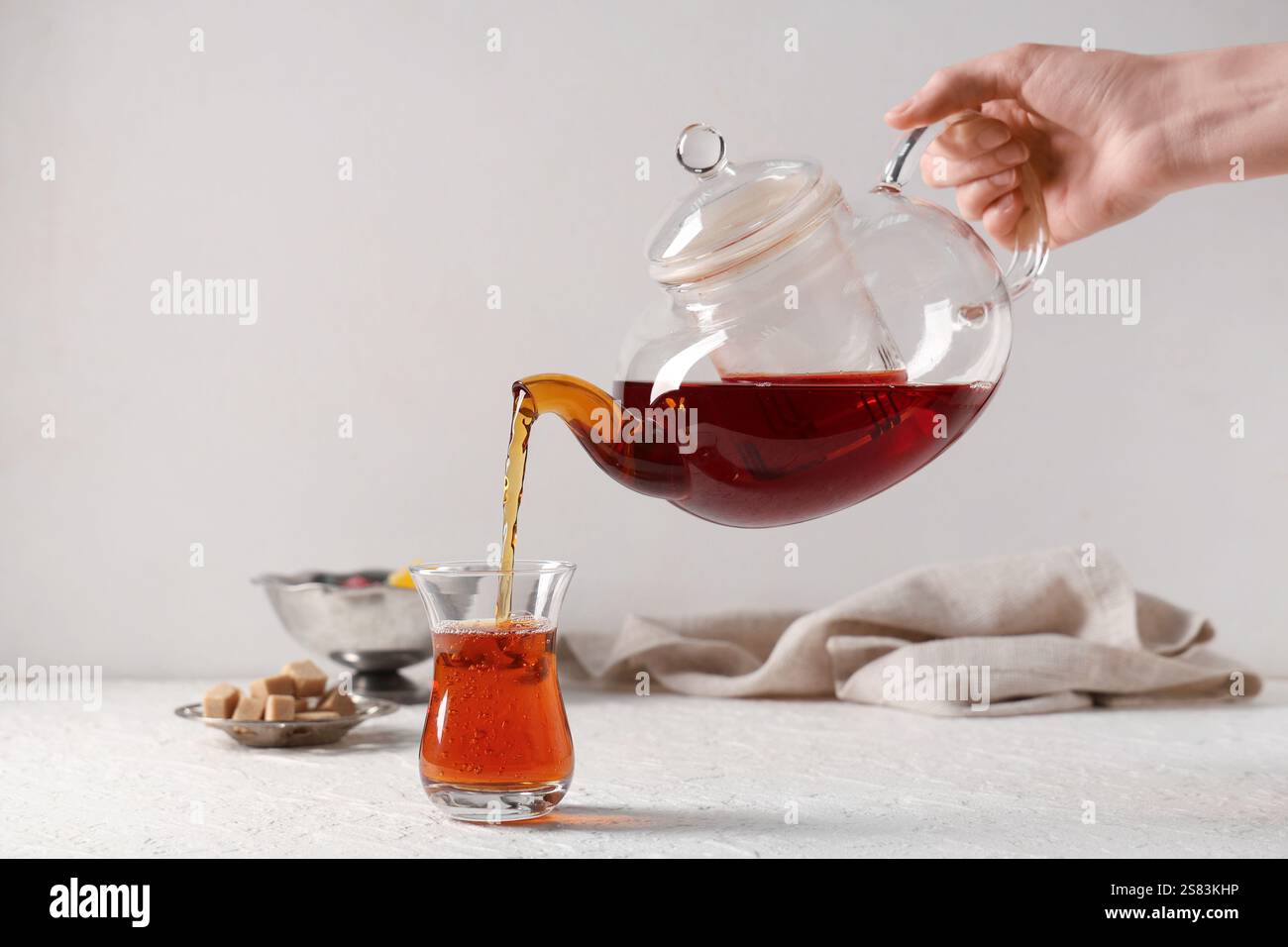 Woman pouring Turkish tea from teapot into glass on white background ...