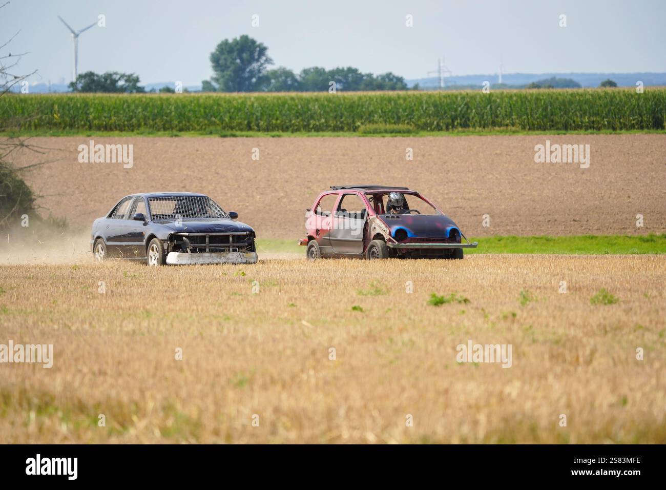 Two cars are racing on a dirt road in a field. One car is black and the ...