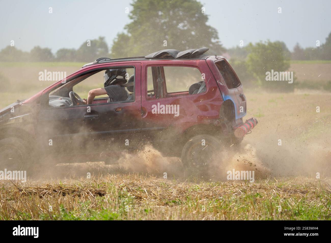 A red car is driving through a field of dirt. The car is covered in mud ...
