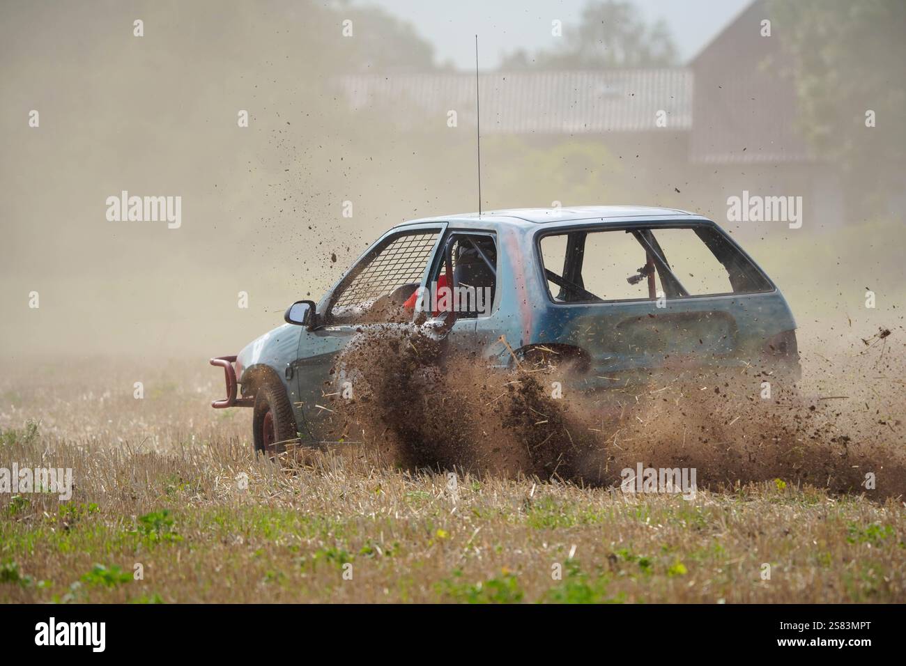A car is driving through a muddy field. The car is covered in mud and ...