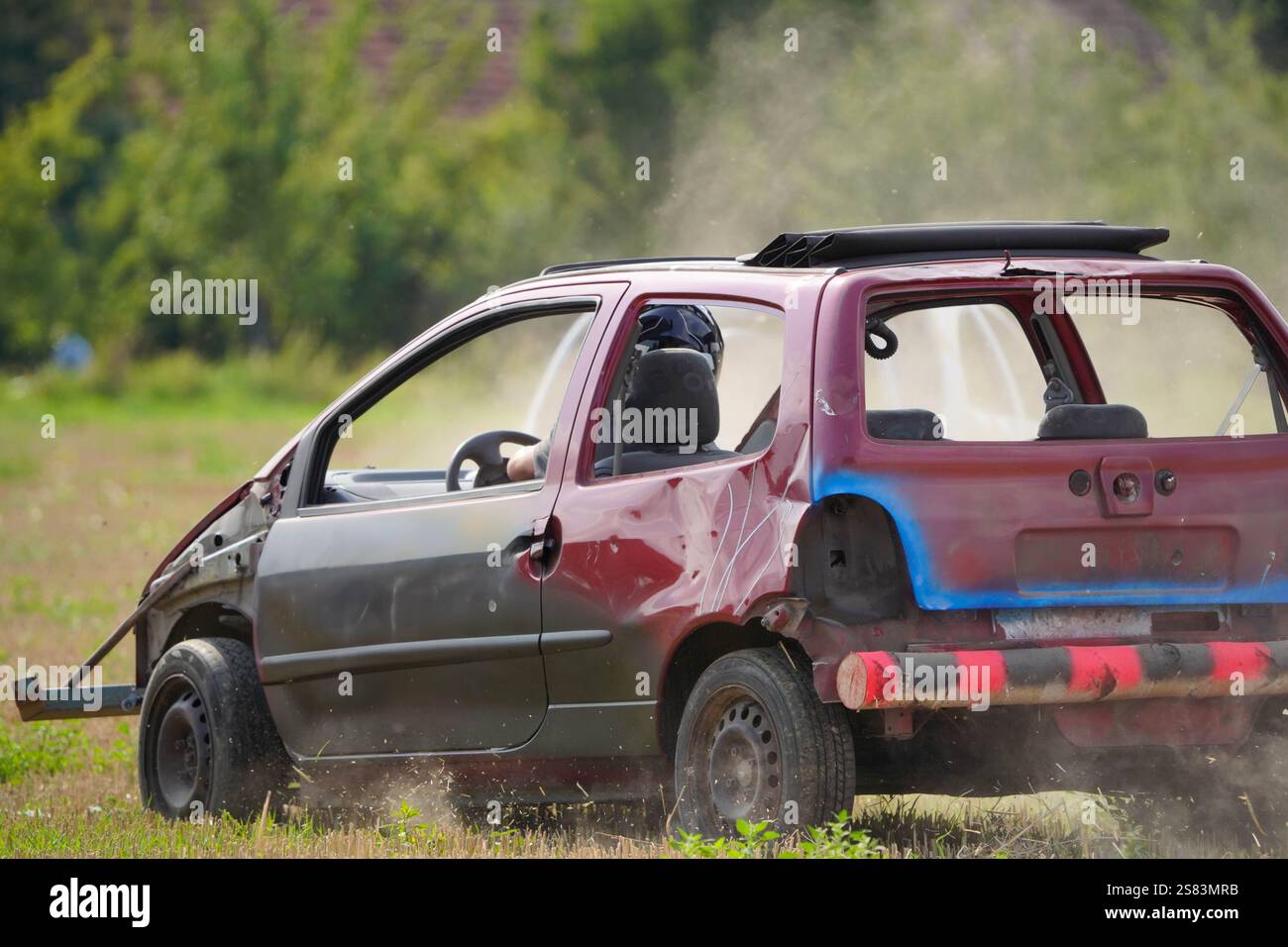 A car is in a junkyard with a man inside. The car is red and has a lot ...