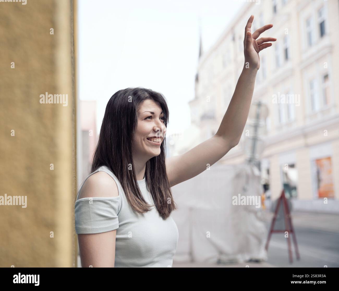 A smiling young woman waving her hand while standing in a bright and ...