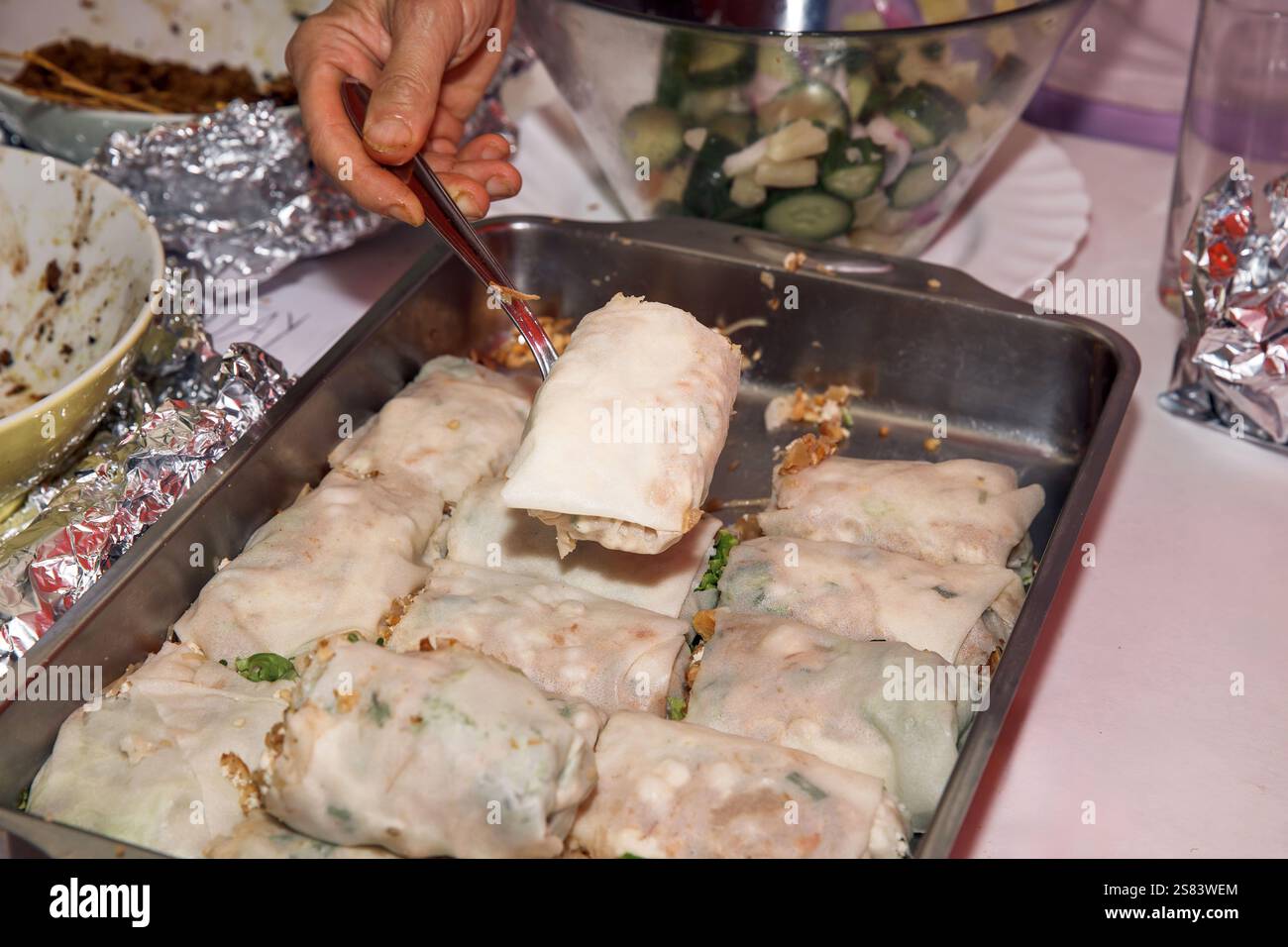 A spoon lifting a single stuffed cabbage roll from a tray filled with ...