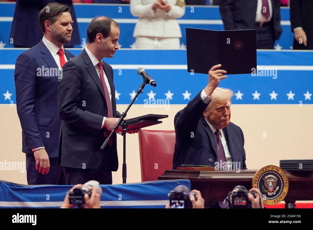 President Donald Trump signs executive orders on stage at an indoor ...