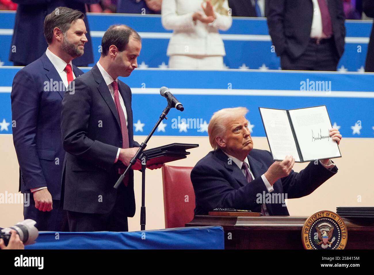 President Donald Trump signs executive orders on stage at an indoor ...