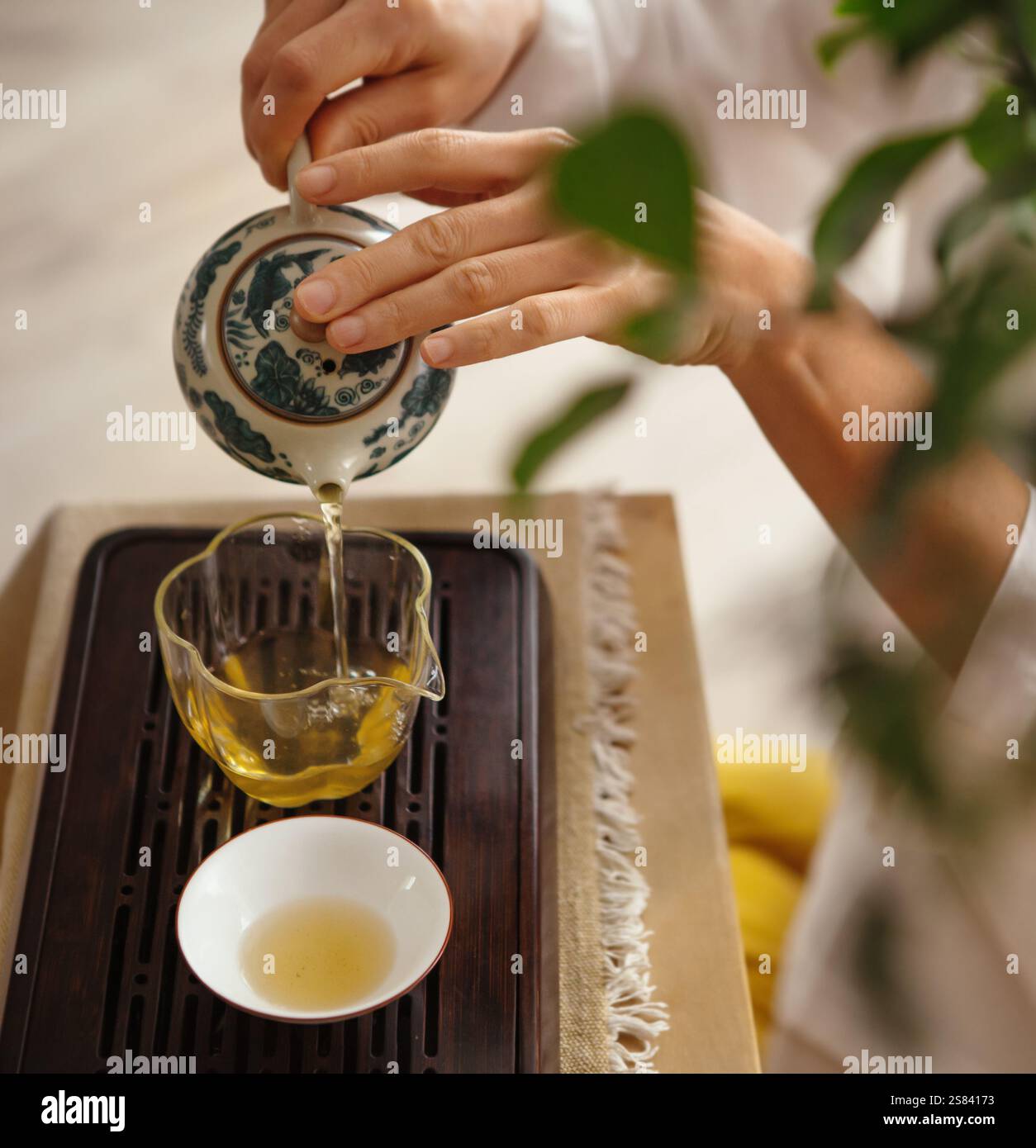 Female hands pouring tea from patterned clay teapot into clear glass ...