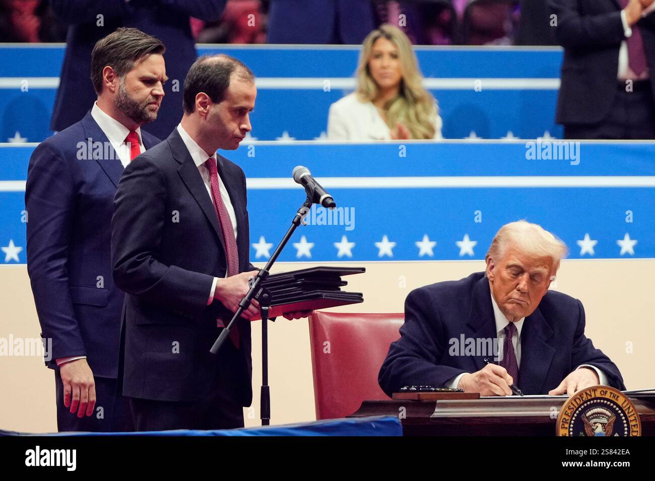 President Donald Trump signs executive orders on stage at an indoor ...