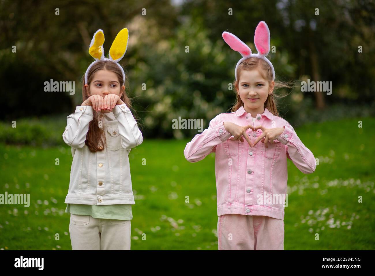 Two young girls wearing colorful bunny ears pose happily in a green ...