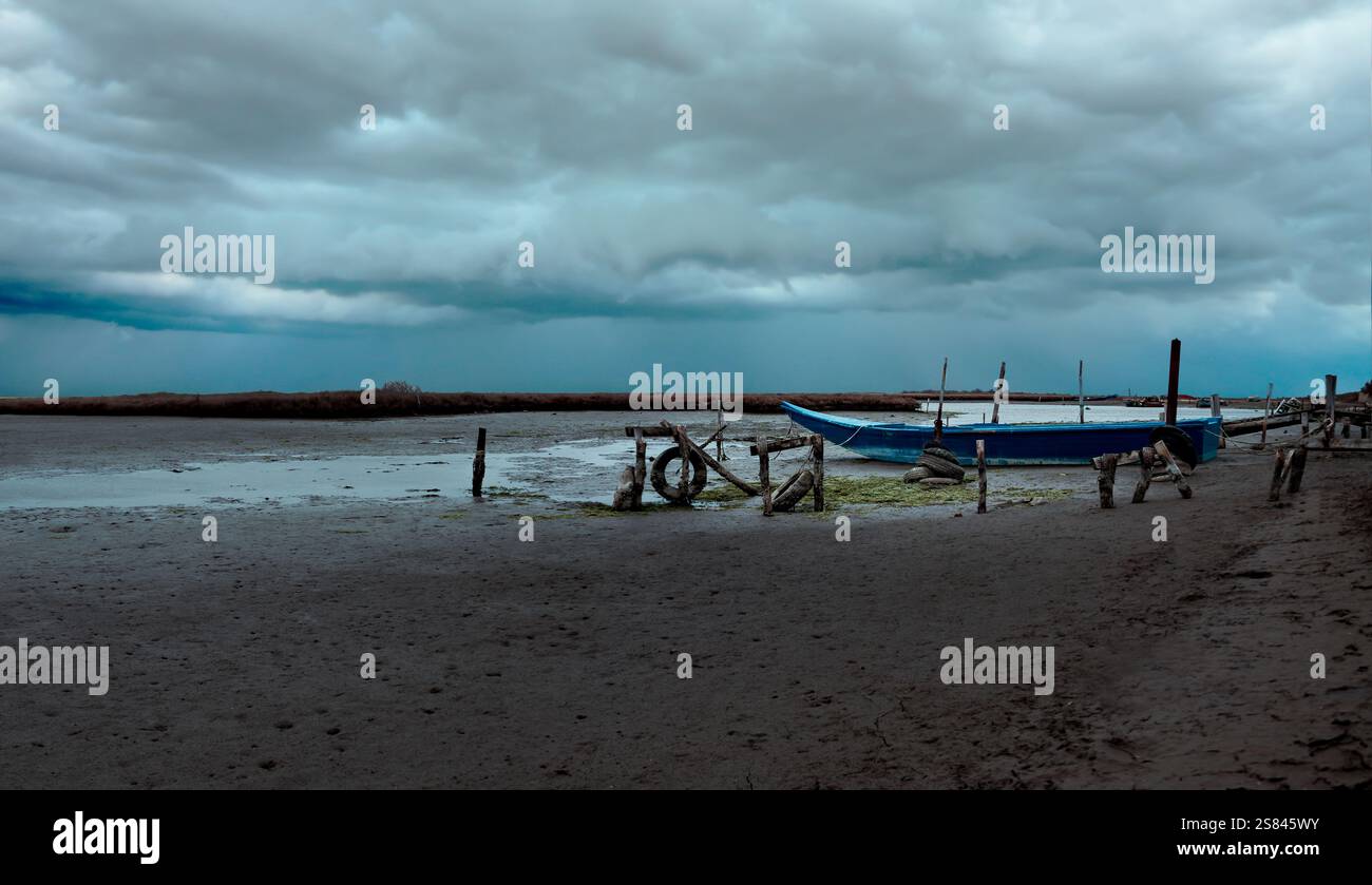 A small blue boat rests in muddy shallow water, surrounded by wooden ...
