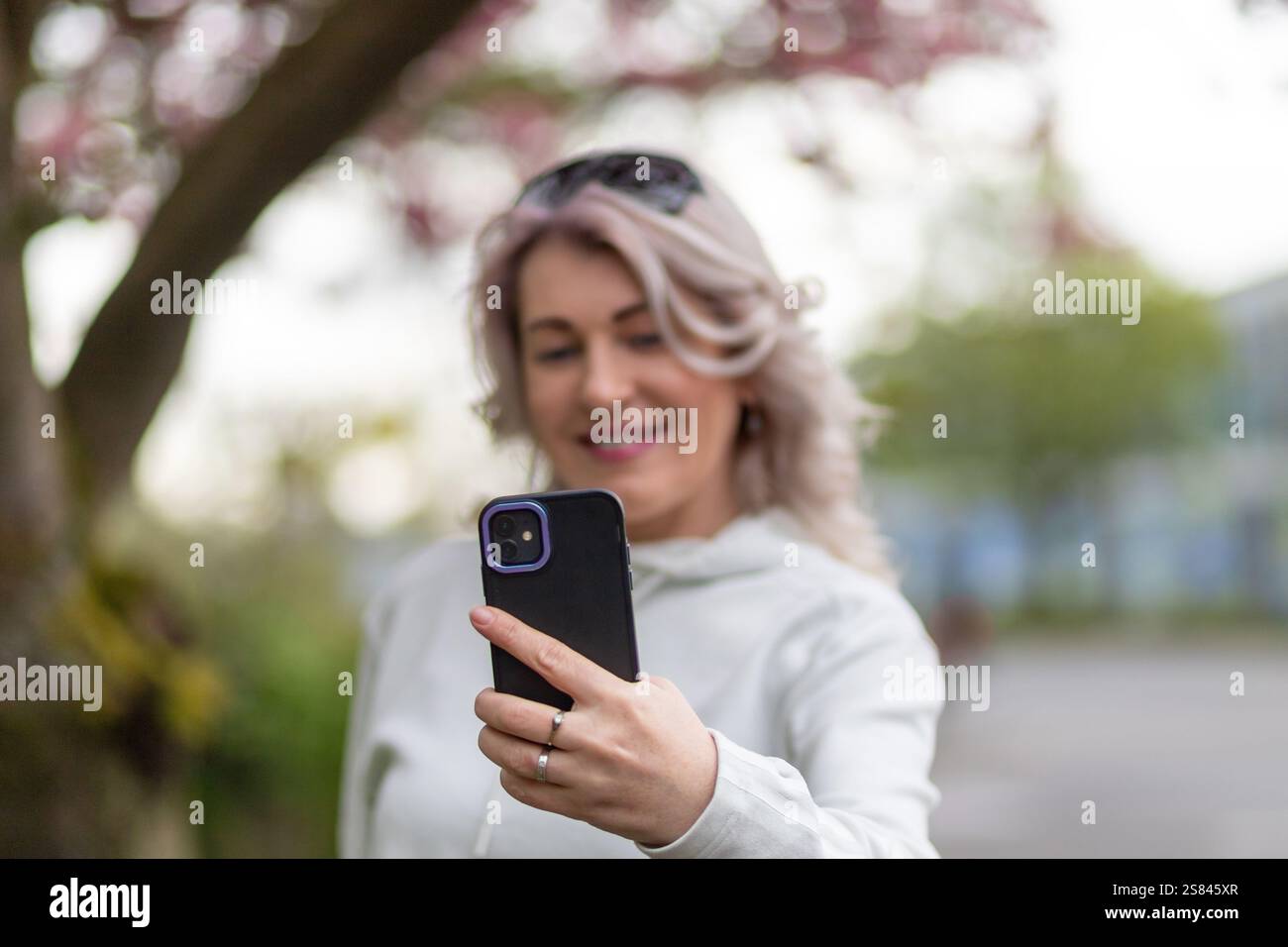 A woman stands in a park surrounded by blooming trees, smiling as she ...