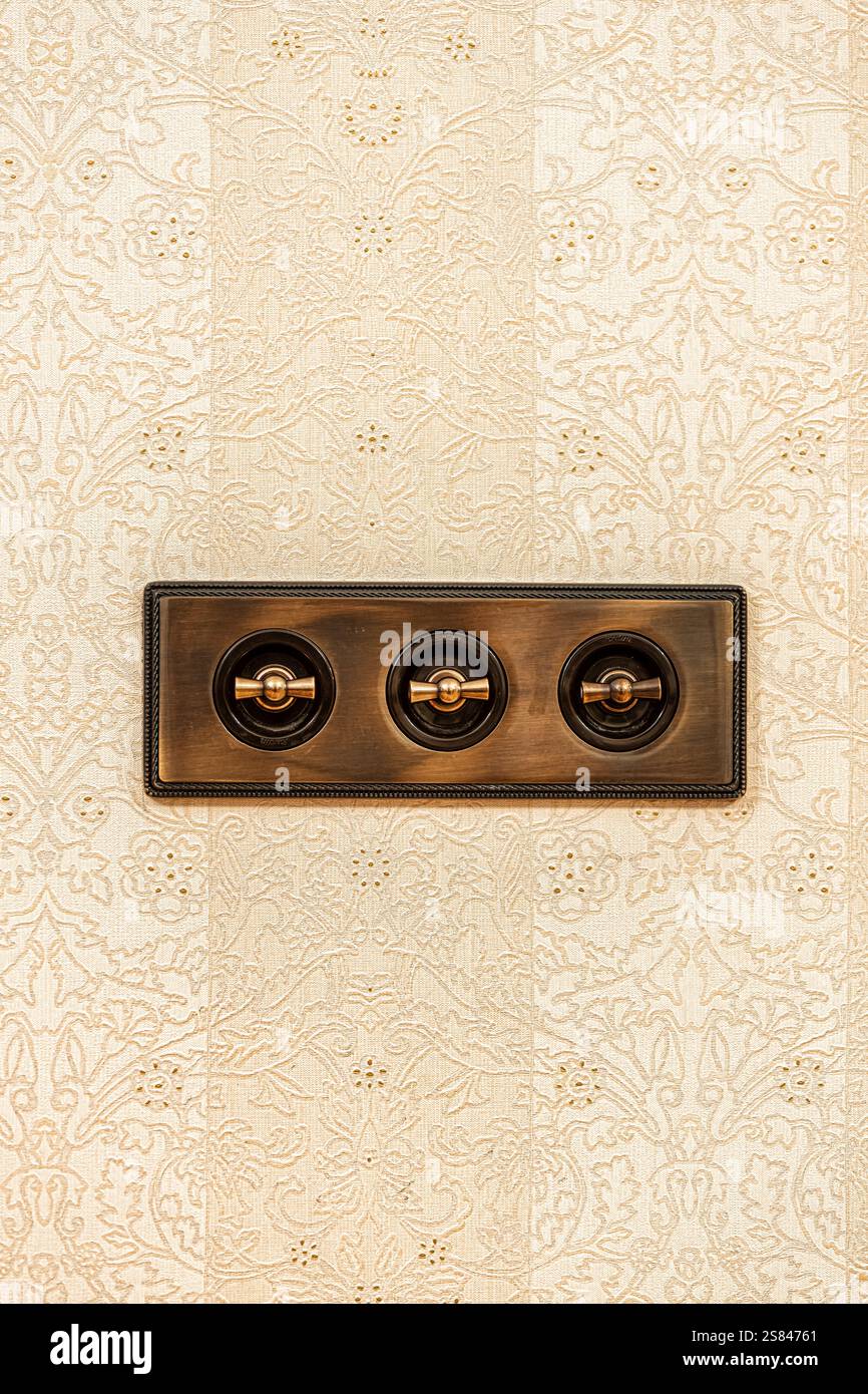 A brass triple toggle light switch panel with rounded toggles mounted ...