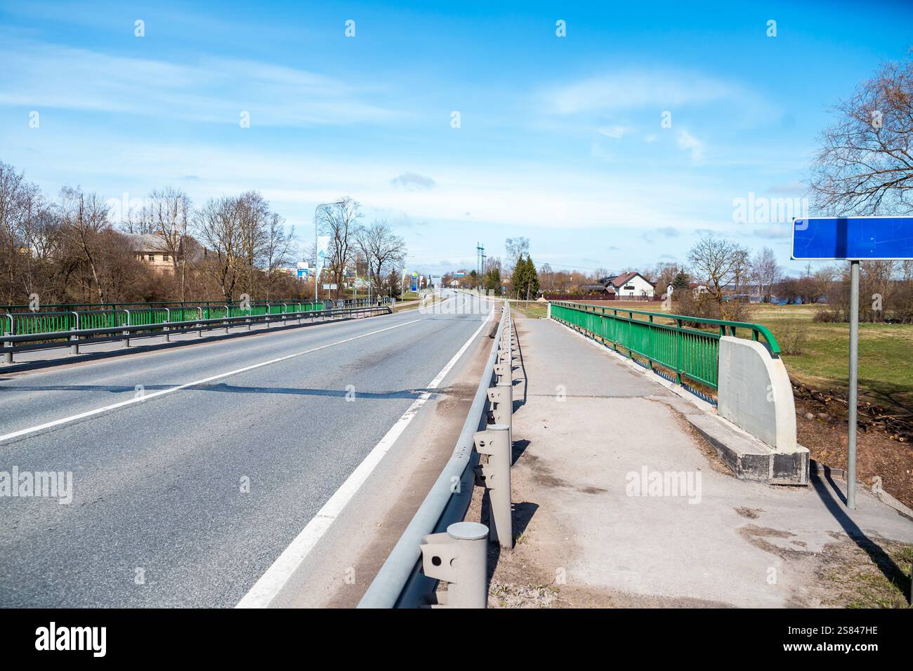 A paved road crossing a small bridge with a pedestrian walkway, green ...