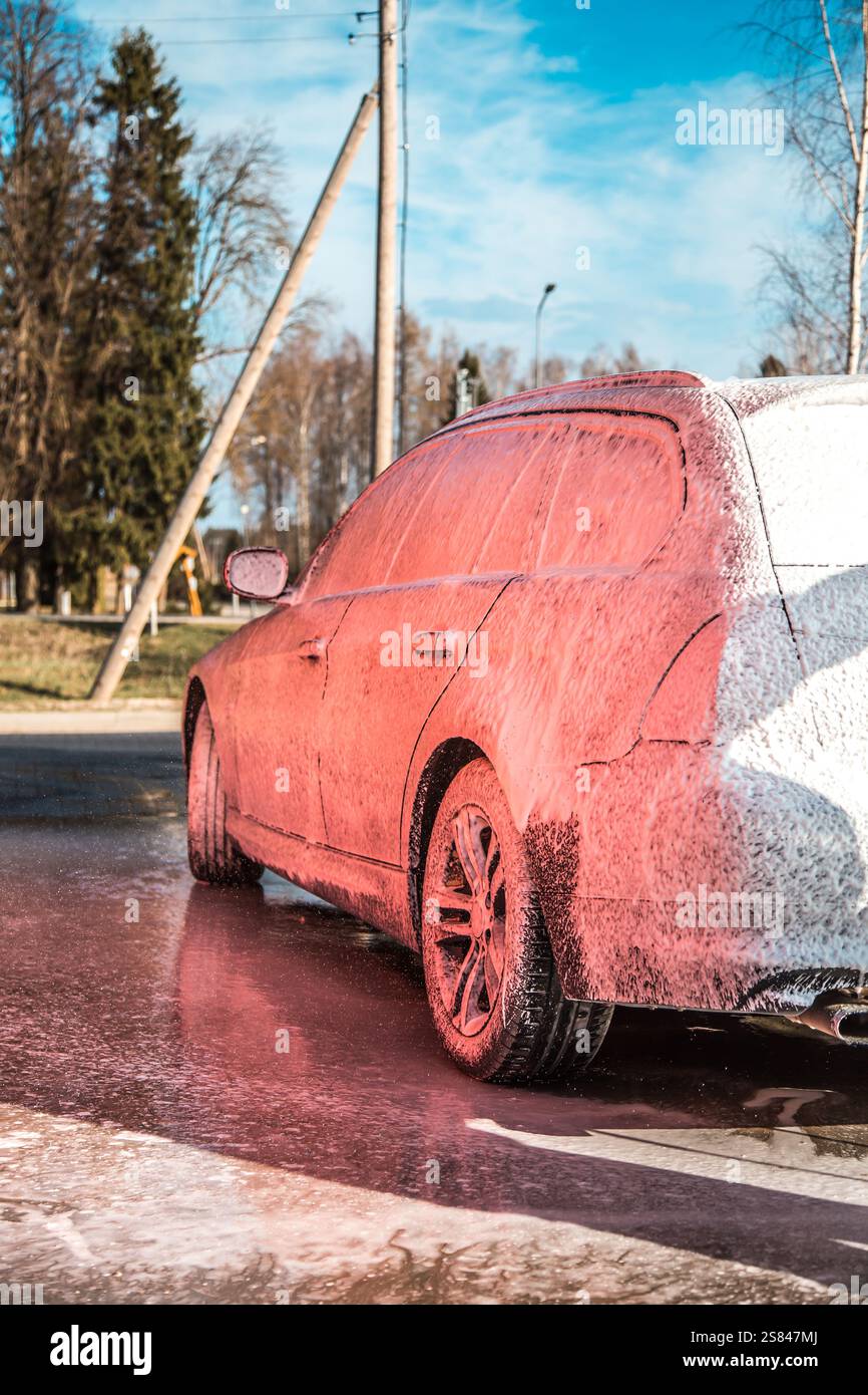 A red car mid cleaning with soap foam covering its surface, set against ...