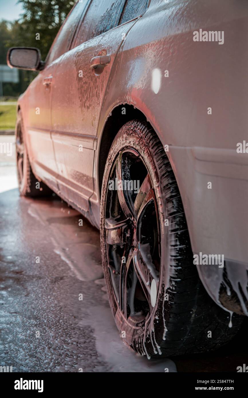 Rear view of a car being washed outdoors, with soap suds on black alloy ...