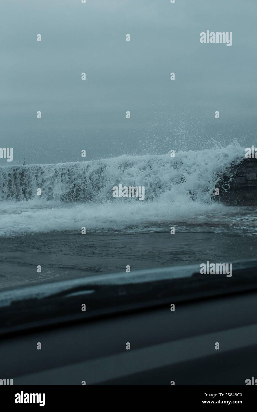 Ocean waves splash against a stone seawall, sending water into the air ...