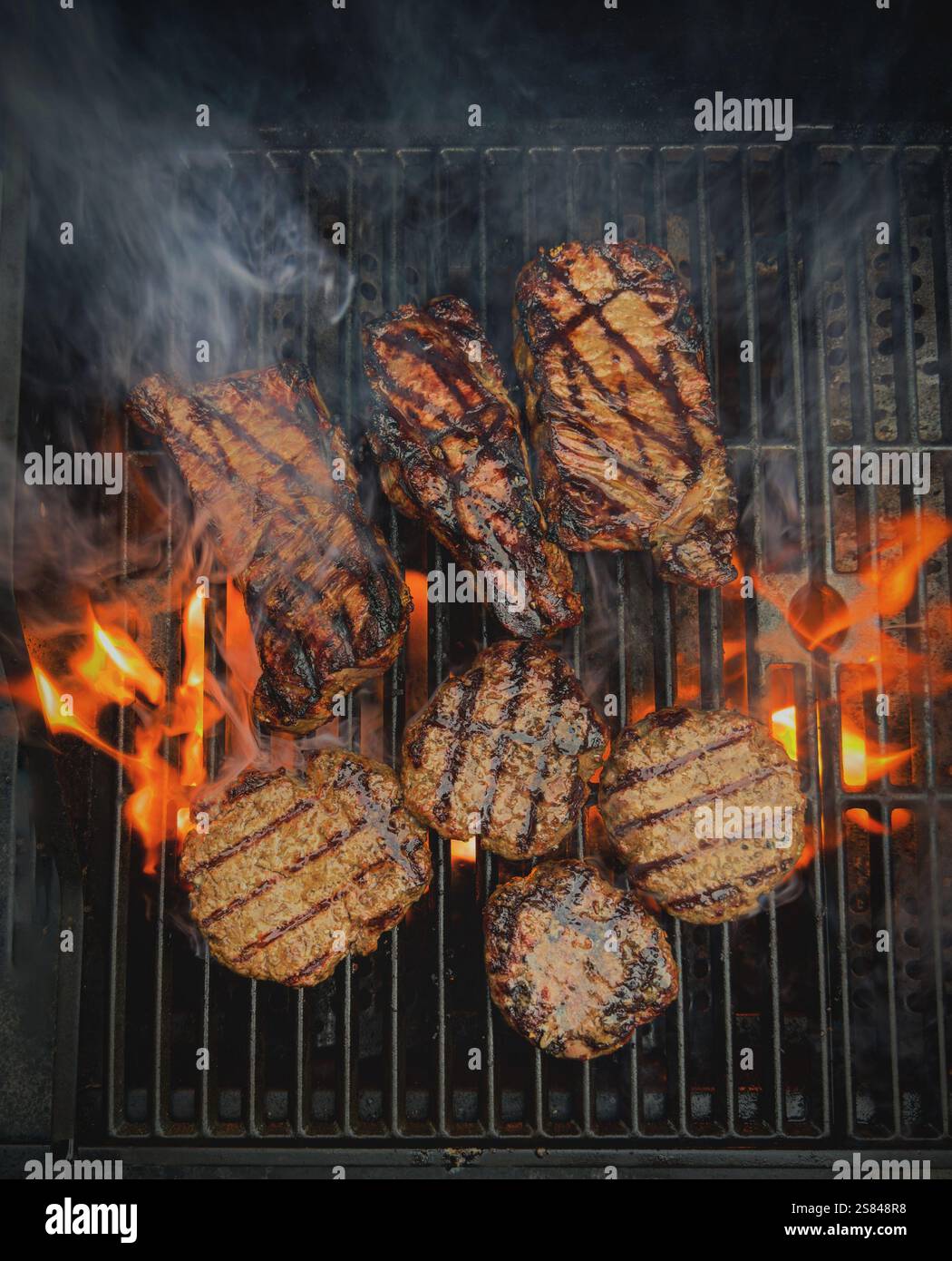 Juicy steaks and burgers sizzling on a fiery barbecue grill with flames ...