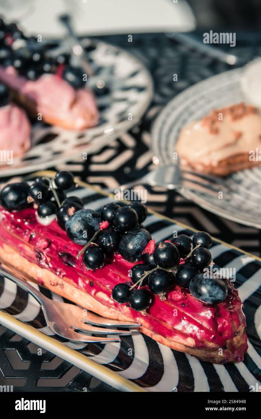 A vibrant eclair topped with blackcurrants and red glaze on a black and ...