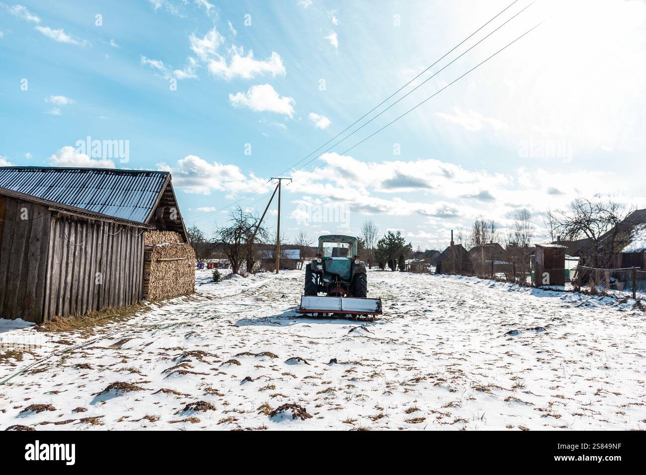 A snow covered field features a tractor, a wooden barn with a metal ...