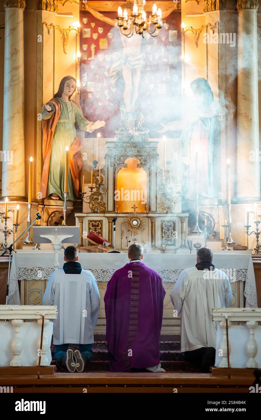 Three individuals in liturgical robes kneel in prayer before a gold ...