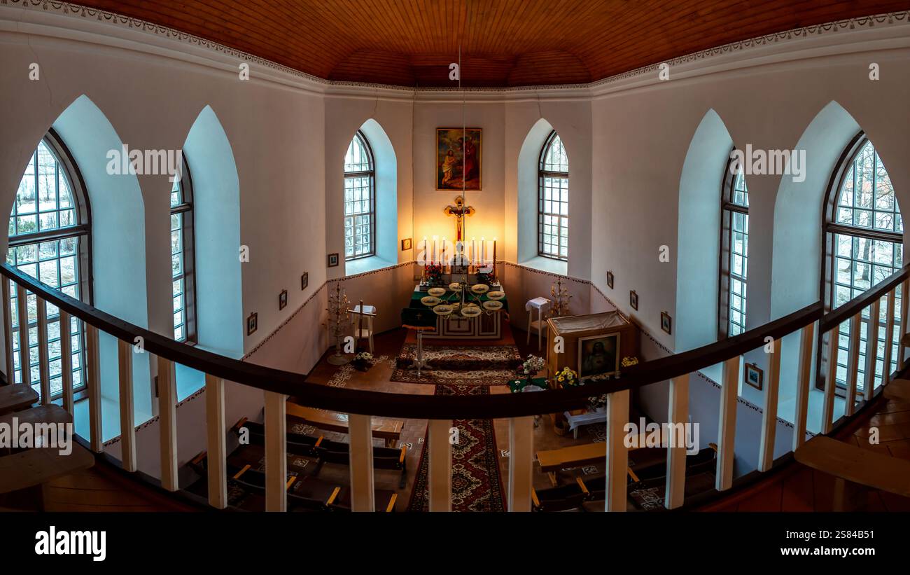 View from a balcony of a church interior featuring wooden ceiling, arched windows, pews, an ...