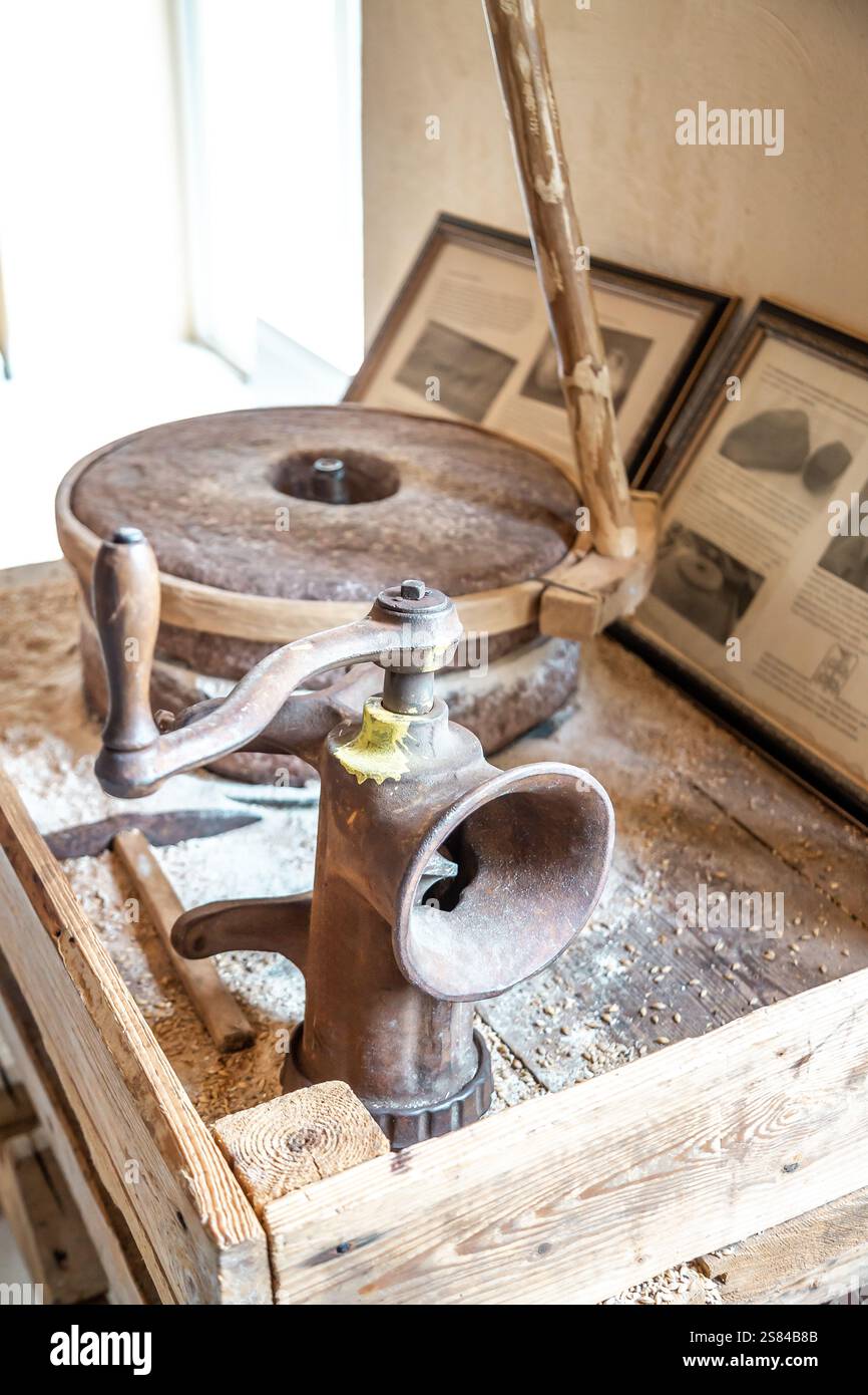 A wooden and metal grain mill with a crank handle, surrounded by grain ...