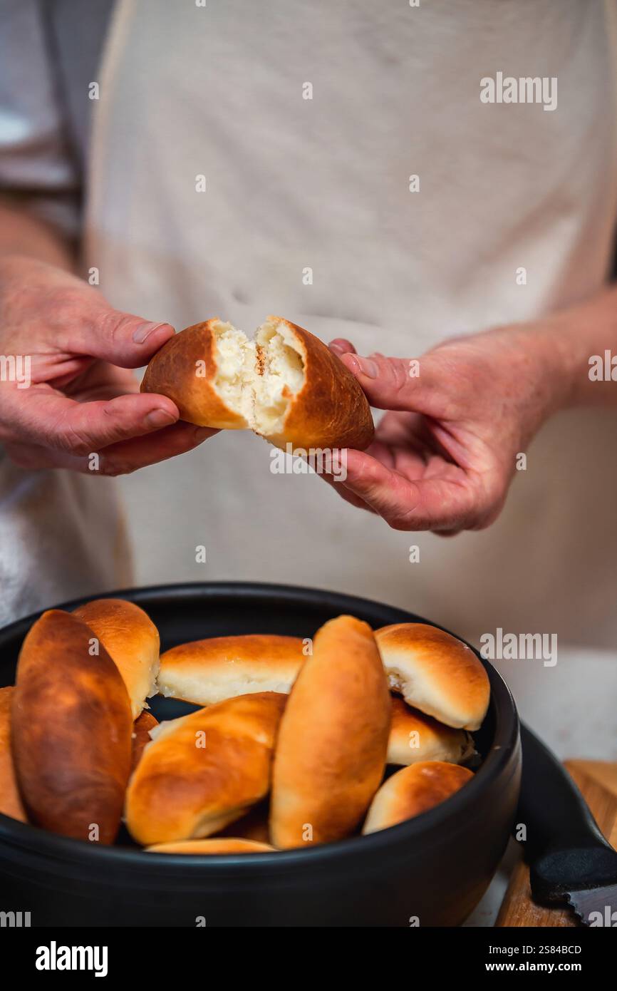 A person in a light colored apron breaks a golden brown bread roll ...