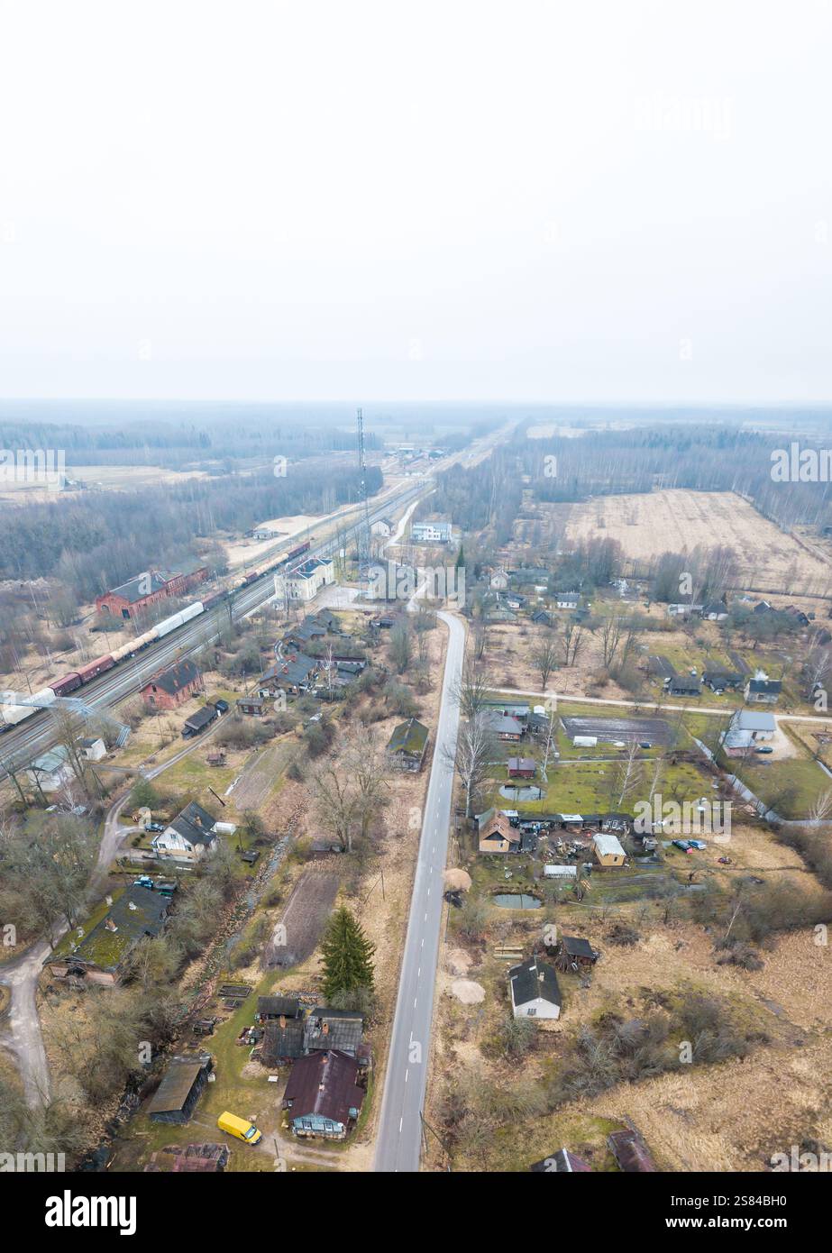 A straight road and railway run parallel through a rural village with ...
